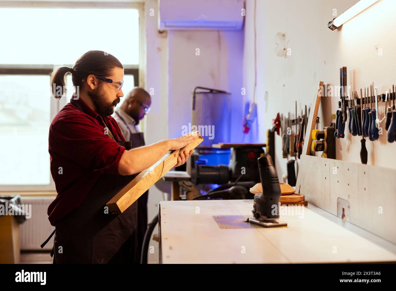 Carpenter wearing protection glasses, checking for scratches on wood ...