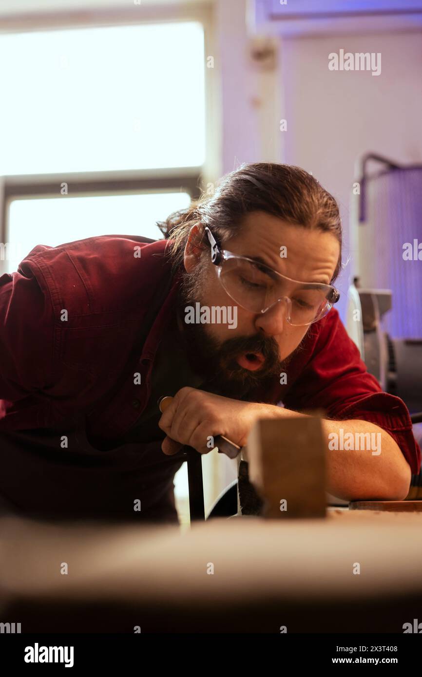 Sculptor blowing sawdust from workbench after shaping raw timber using ...