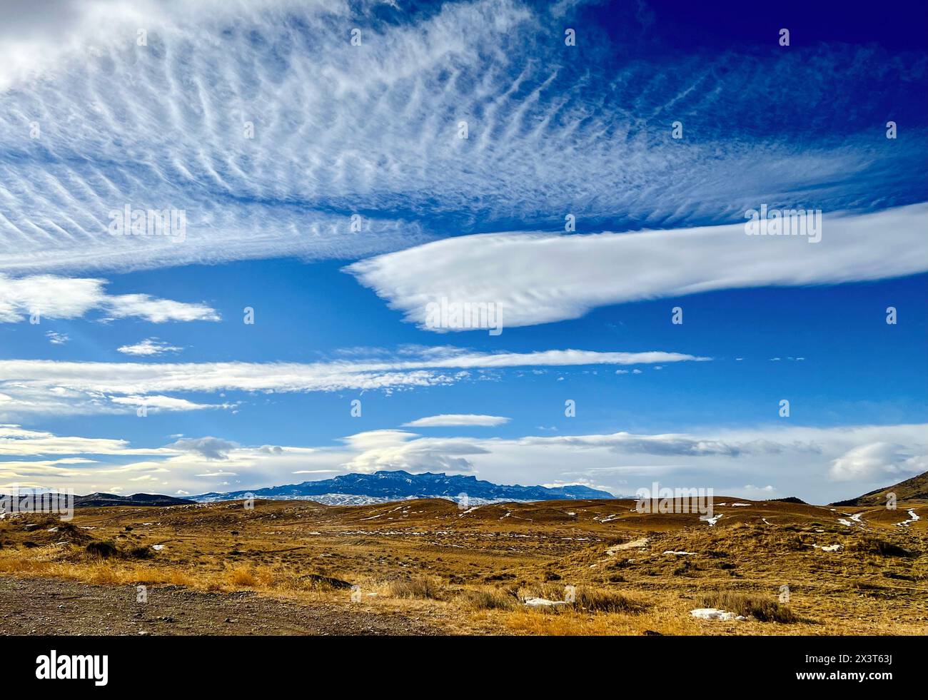 Altocumulus clouds and other cloud formations in deep blue sky hover over Absaroka Mountains in ...