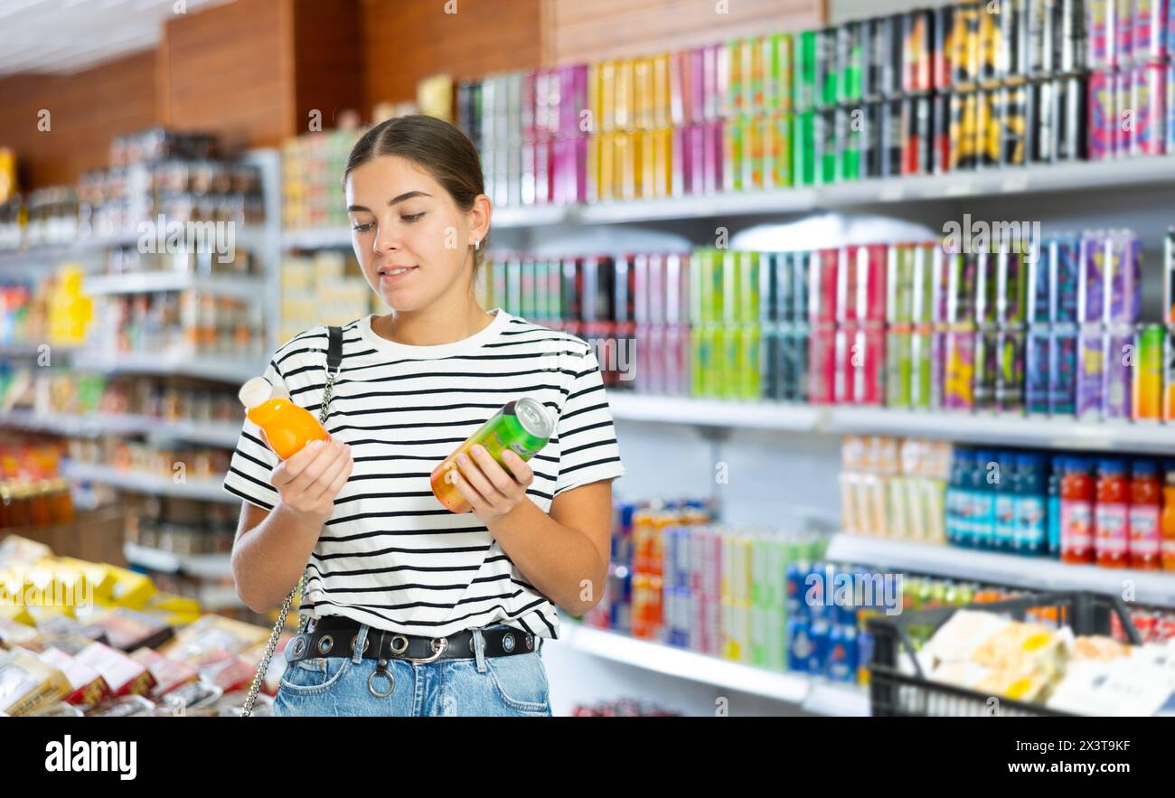 Young girl choosing colored drinks in drinks section of supermarket ...