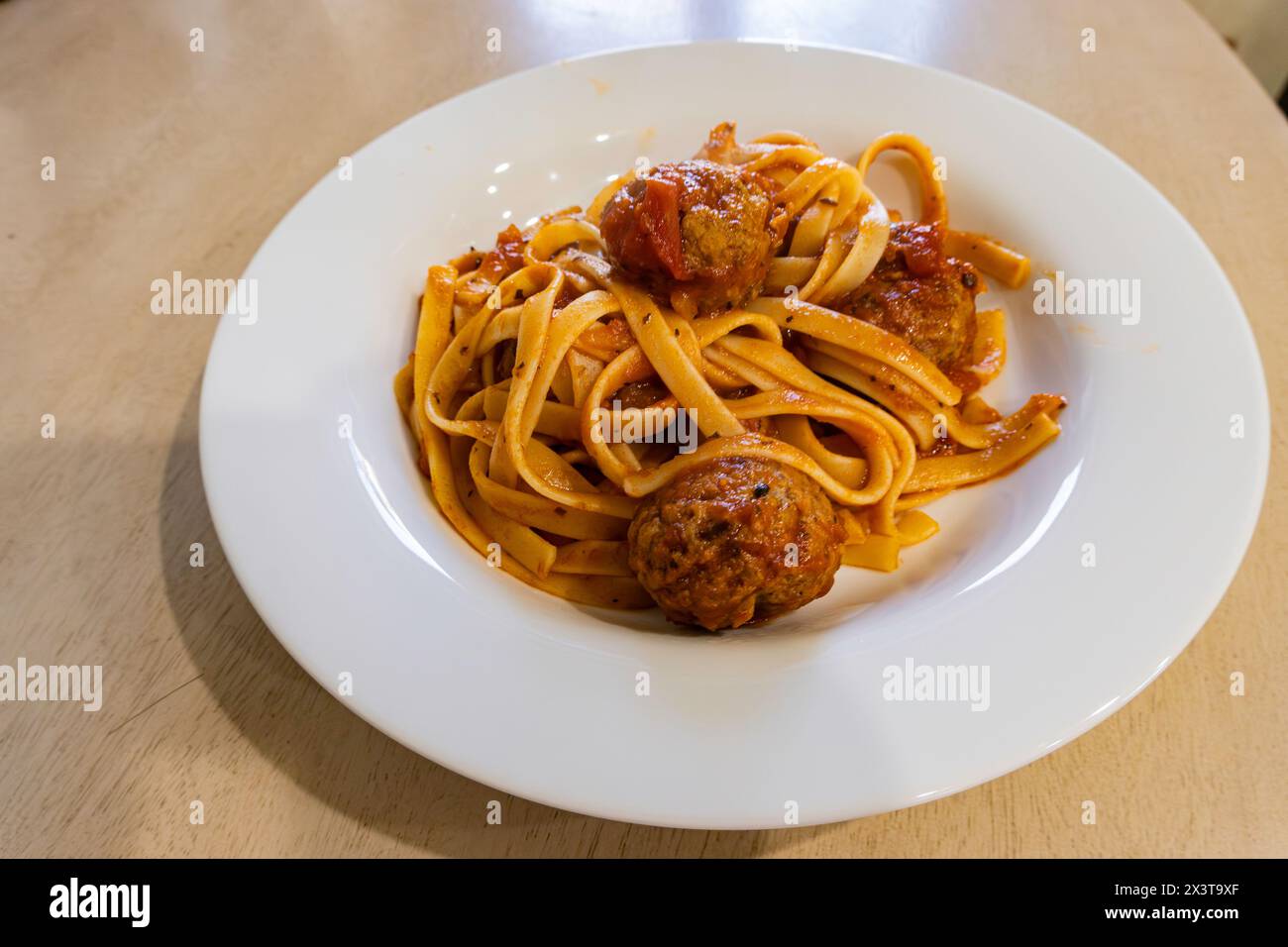 White dish of linguine with spaghetti sauce & meatballs sitting on a ...