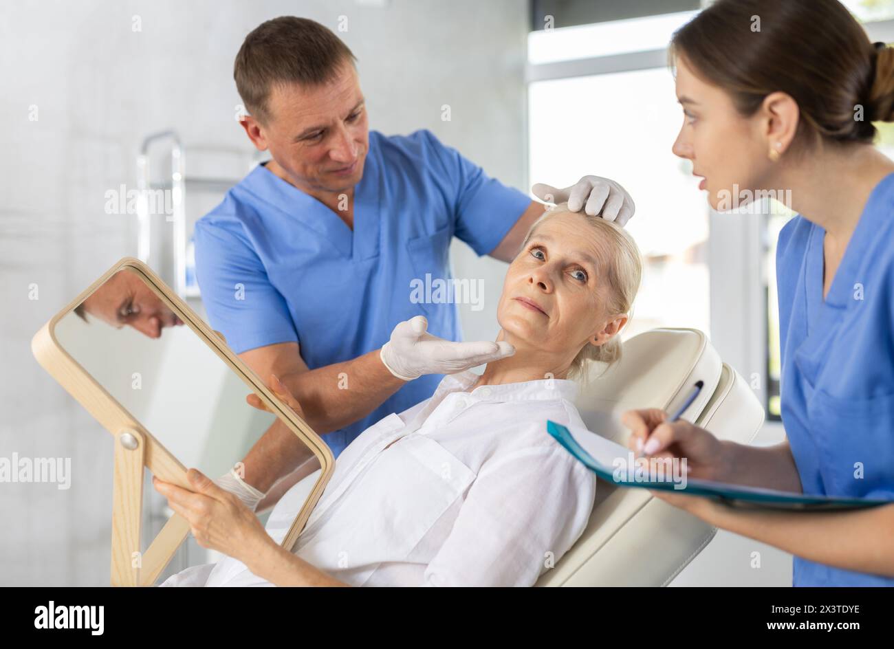 Man dermatologist examines skin of senior womans face, female nurse ...