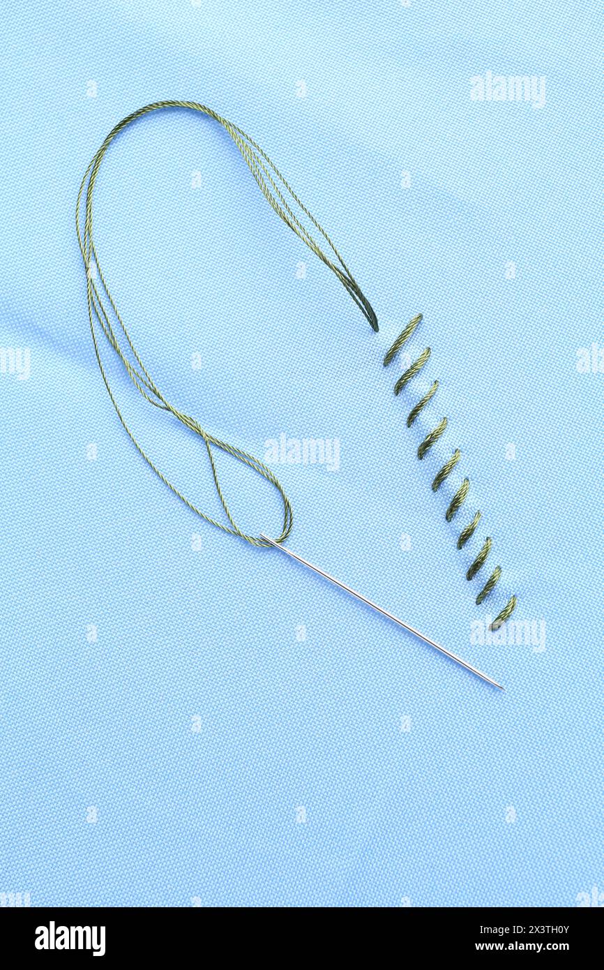 Sewing needle with thread and stitches on light blue cloth, top view ...