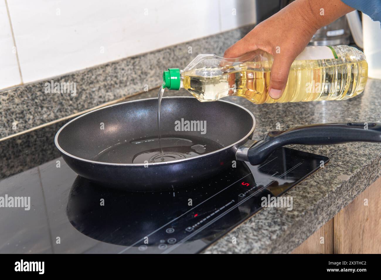 hand putting oil in a frying pan on an induction cooker in the kitchen ...