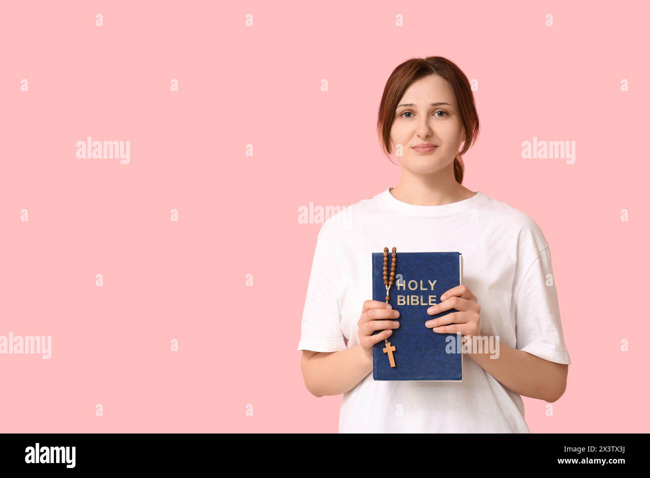 Religious young woman with Holy Bible and rosary beads on pink ...