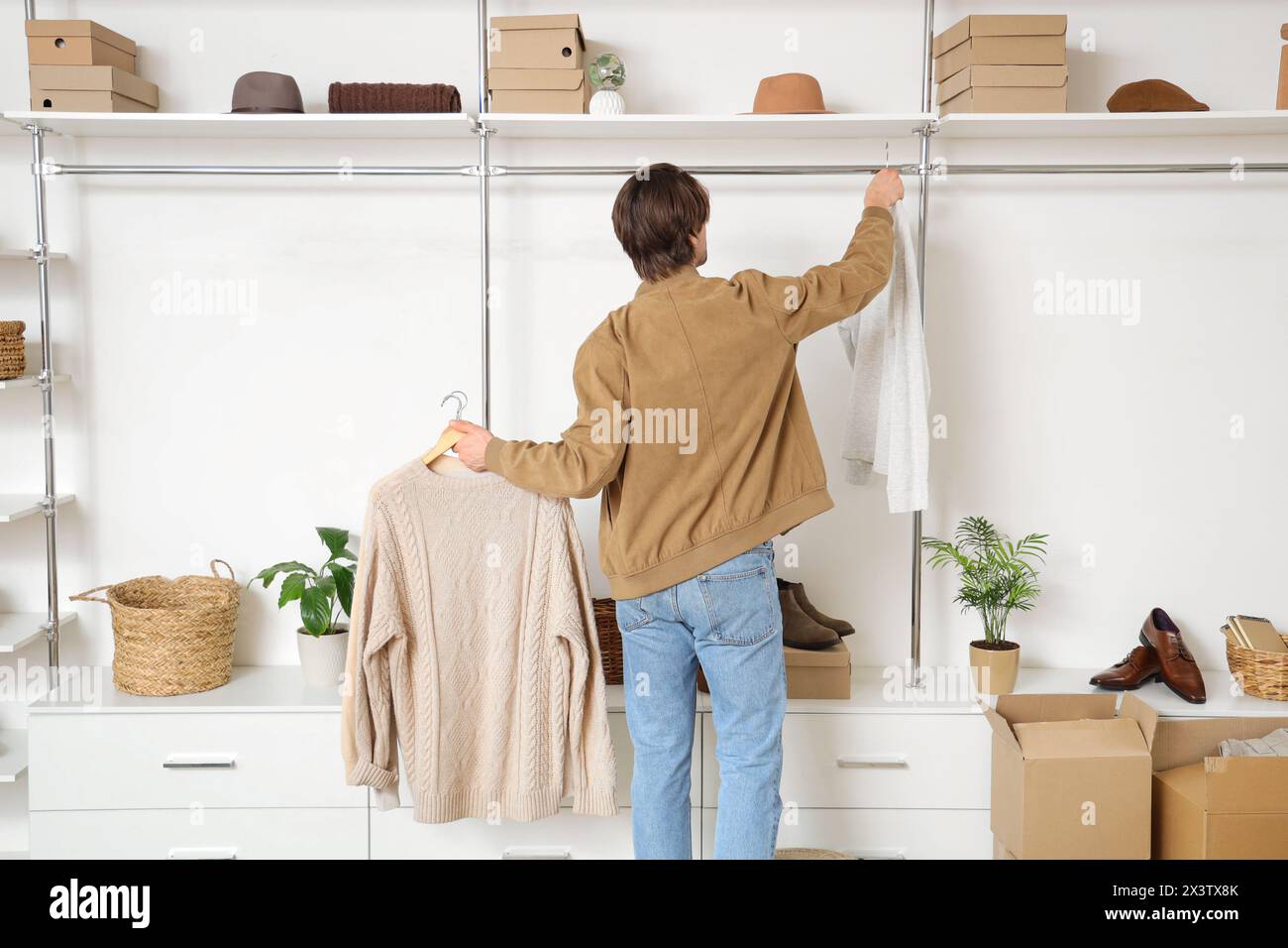 Handsome young man arranging stylish clothes in dressing room, back ...