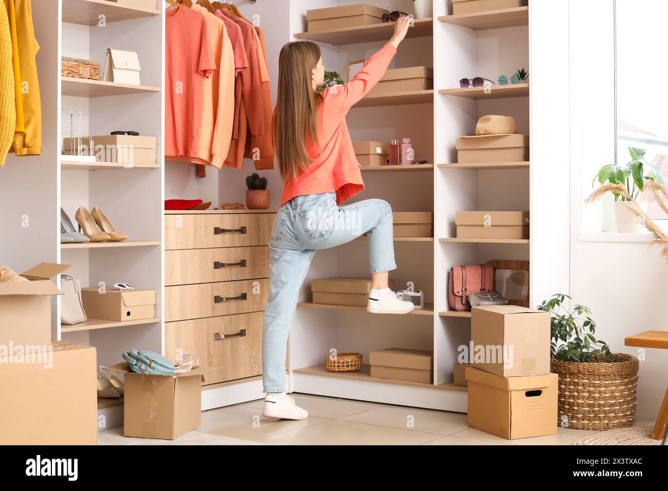 Beautiful young woman with wardrobe boxes arranging clothes in dressing ...