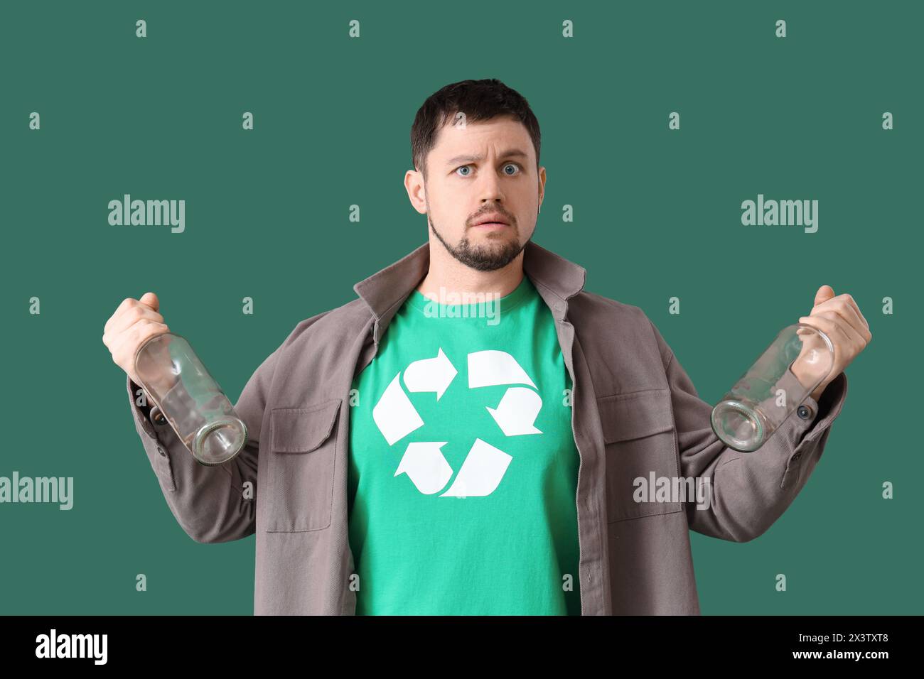 Confused young man in t-shirt with recycling logo holding glass bottles ...