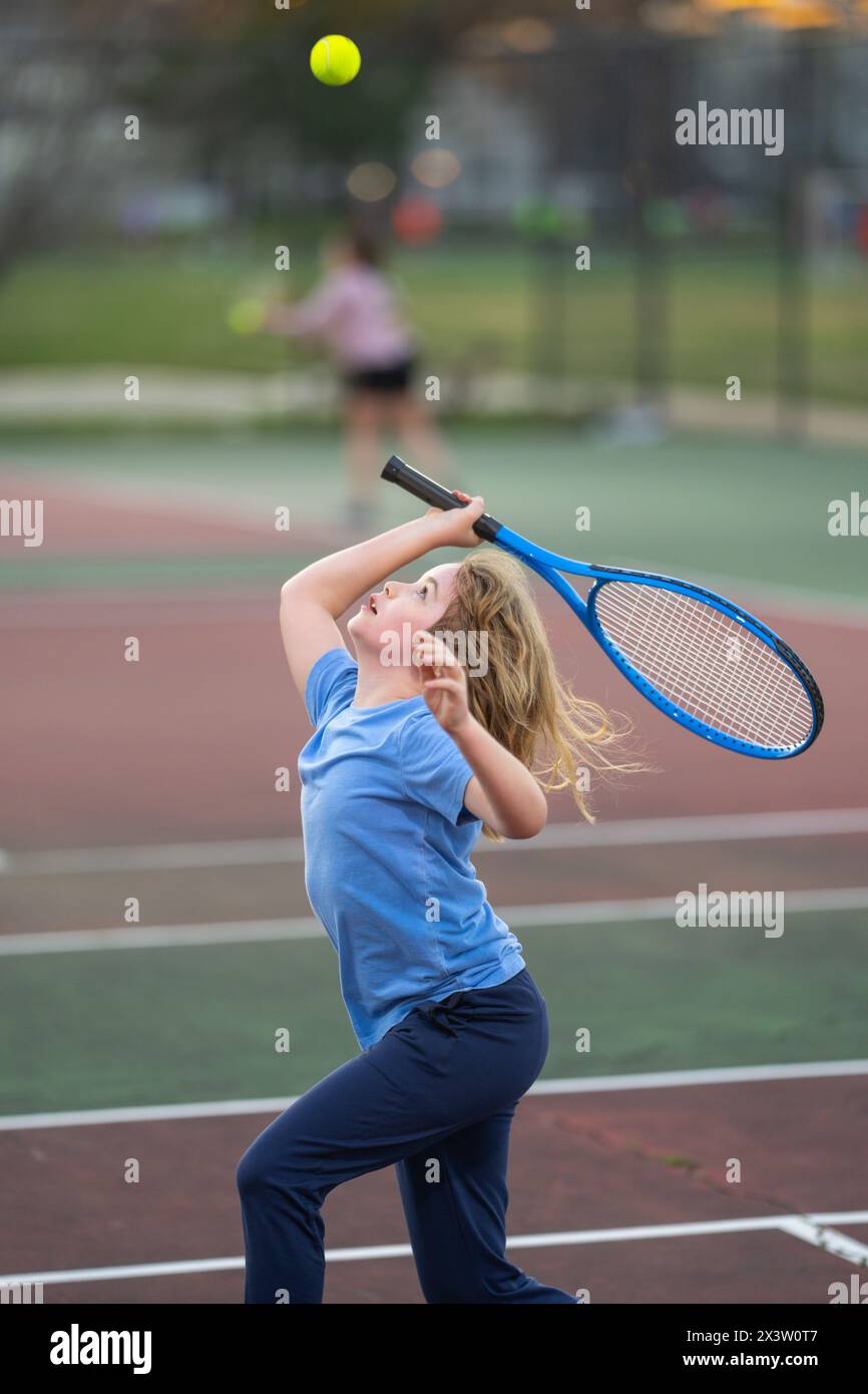 Preteen child swinging racket while training on tennis court at sport ...