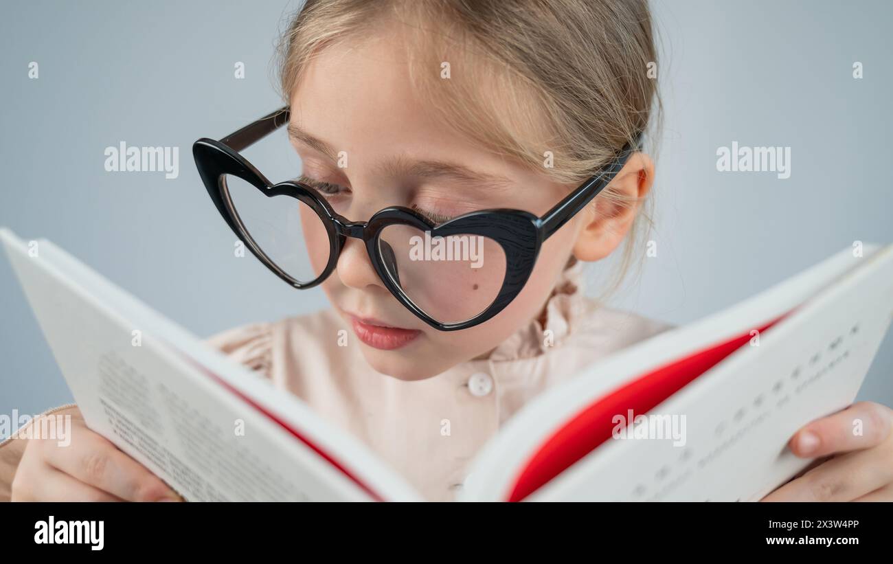 Portrait of a little girl in heart-shaped glasses reading a book Stock ...