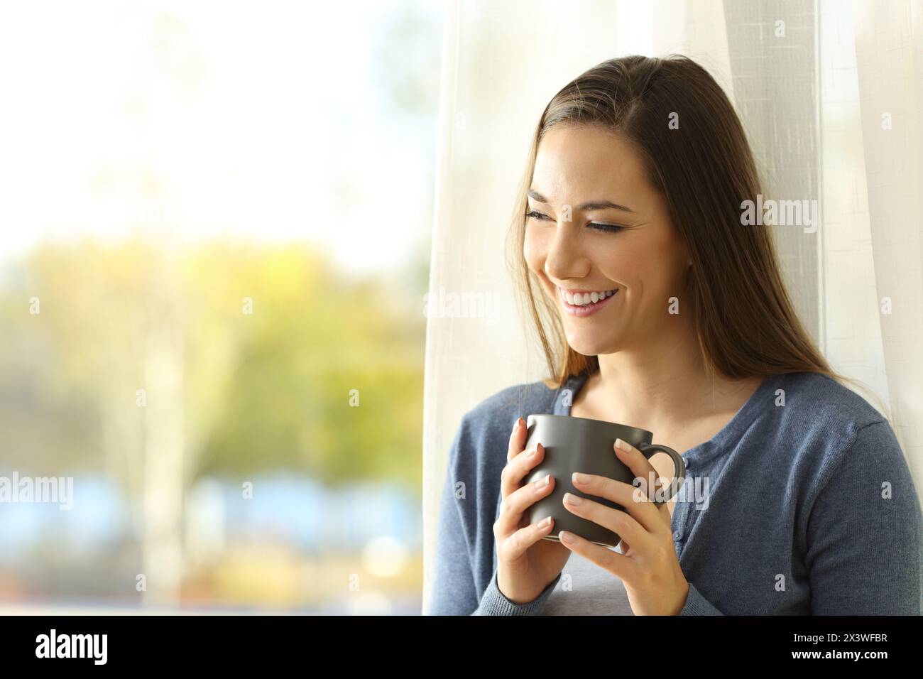 Happy pensive tenant drinking coffee beside a window at home Stock ...