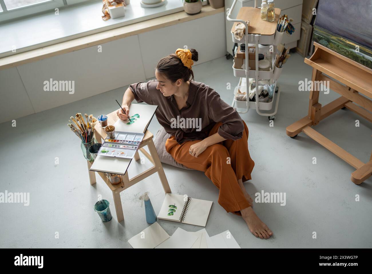Top view of focused woman artist sitting on floor in art studio ...