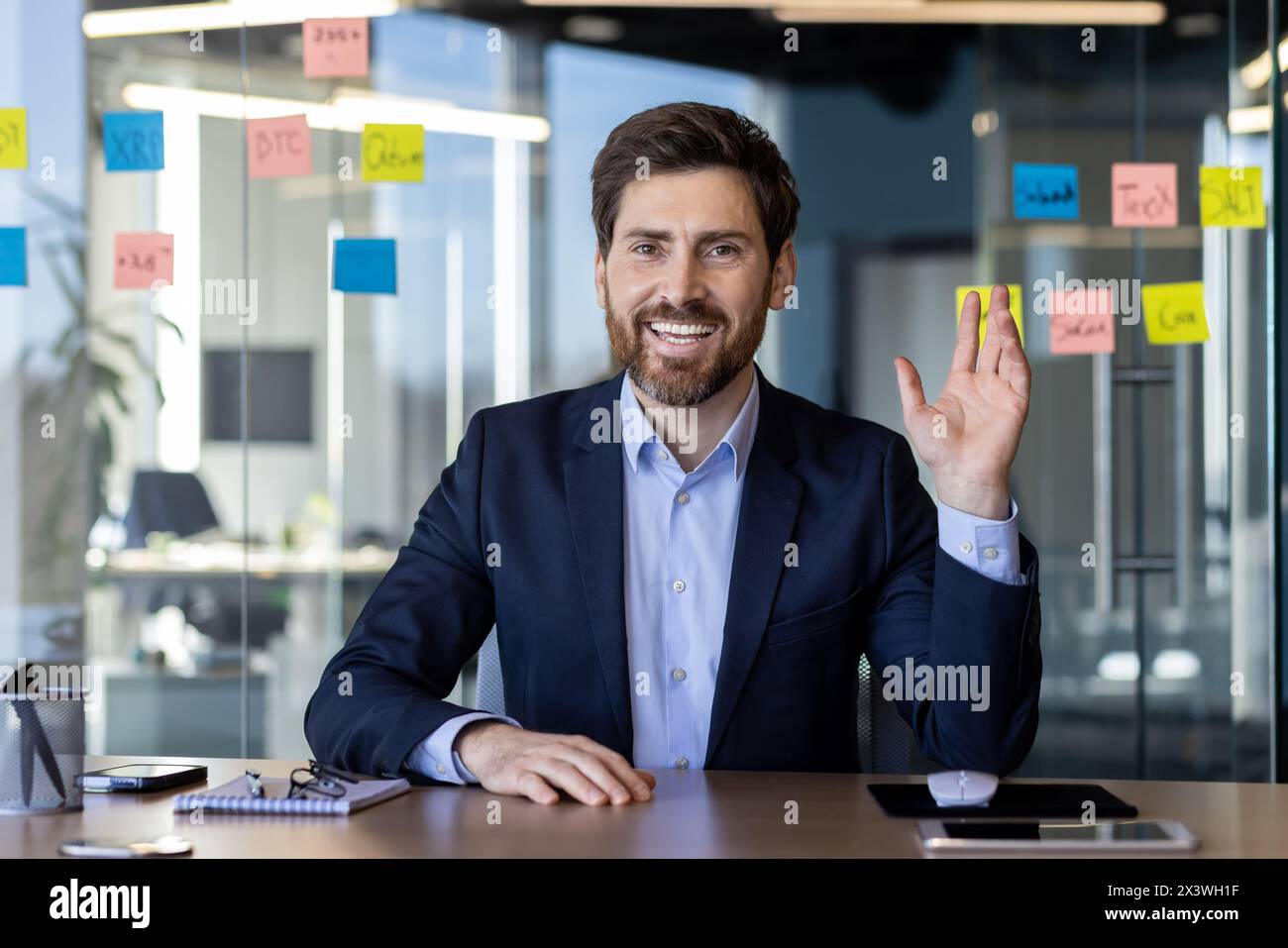 Professional male in a suit waves at the camera during a video call ...