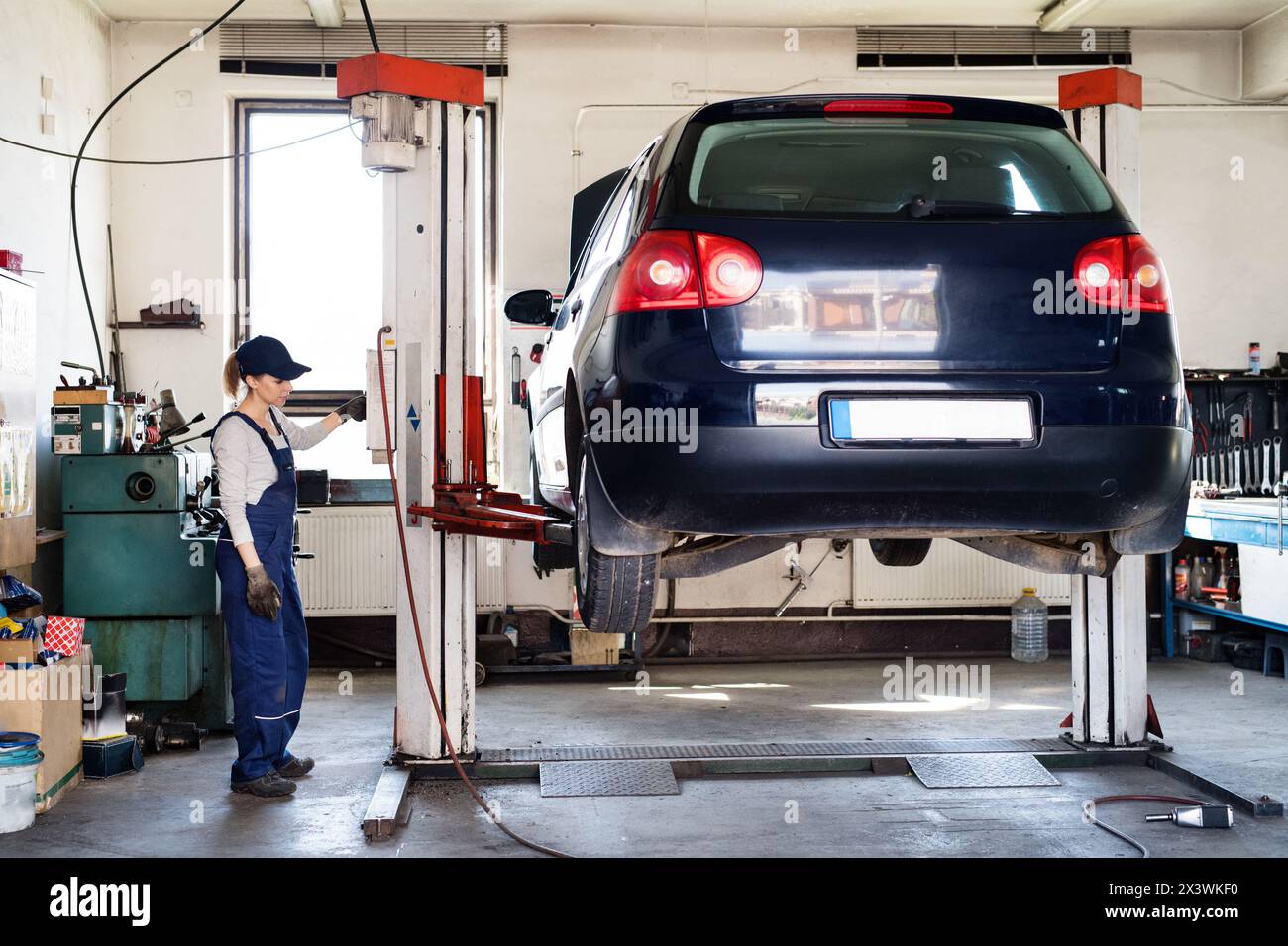 Female auto mechanic elevating car on car lift, working underneath ...