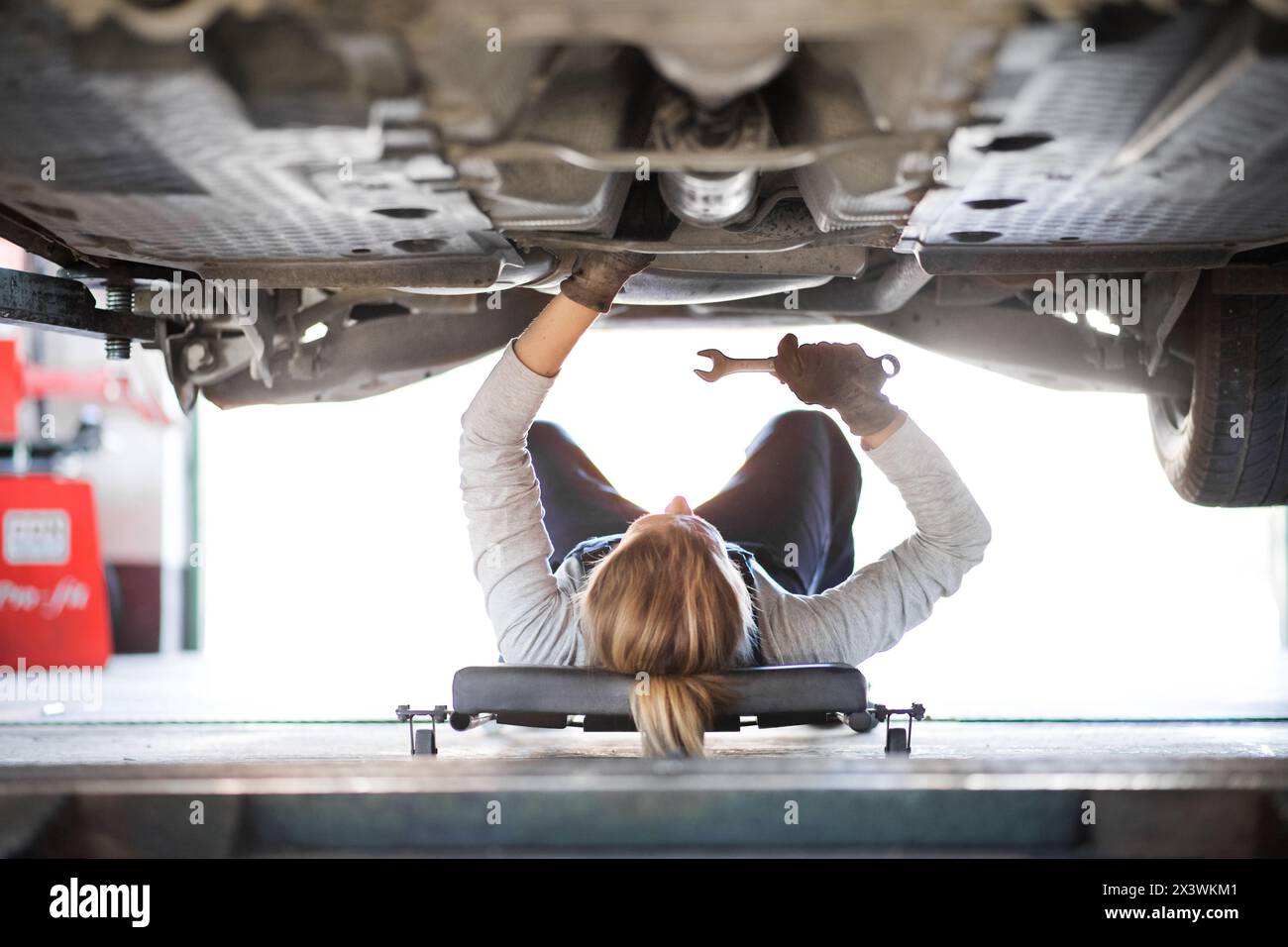 Female auto mechanic lying on mechanic creeper under car, inspecting ...