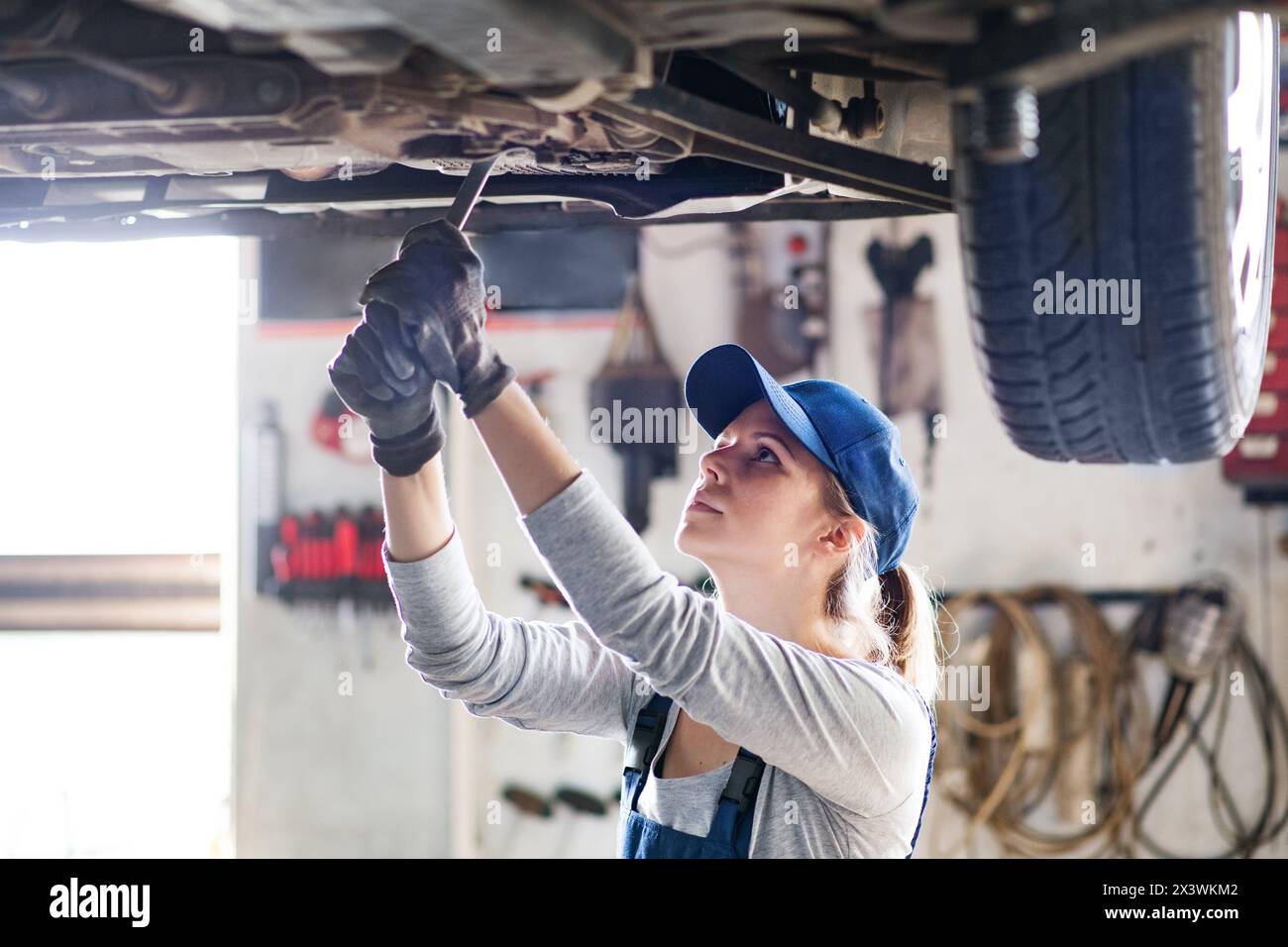 Female auto mechanic elevating car on car lift, working underneath ...