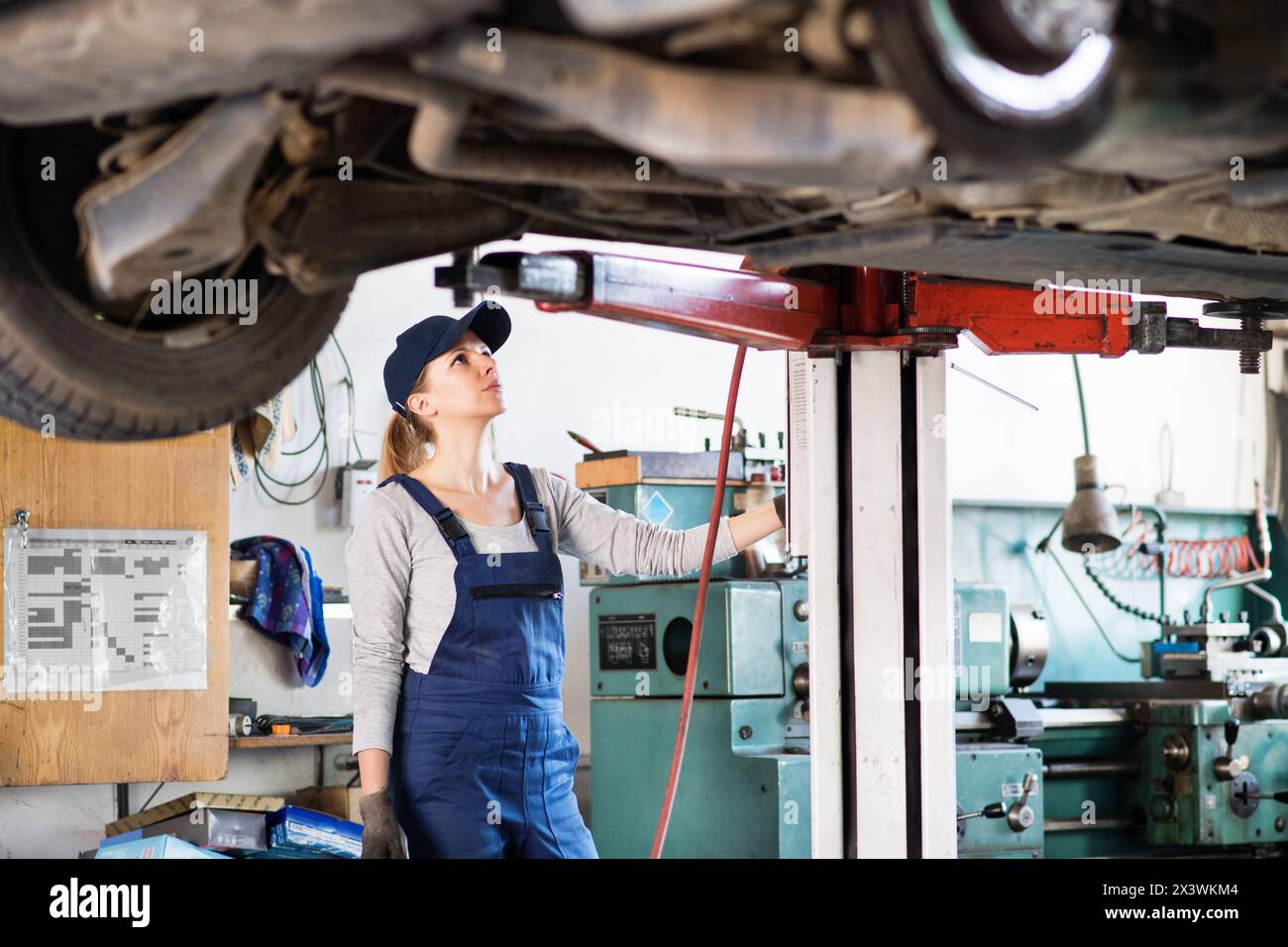 Female auto mechanic elevating car on car lift, working underneath ...