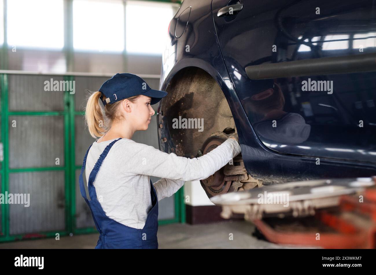 Female auto mechanic elevating car on car lift, checking breaks ...