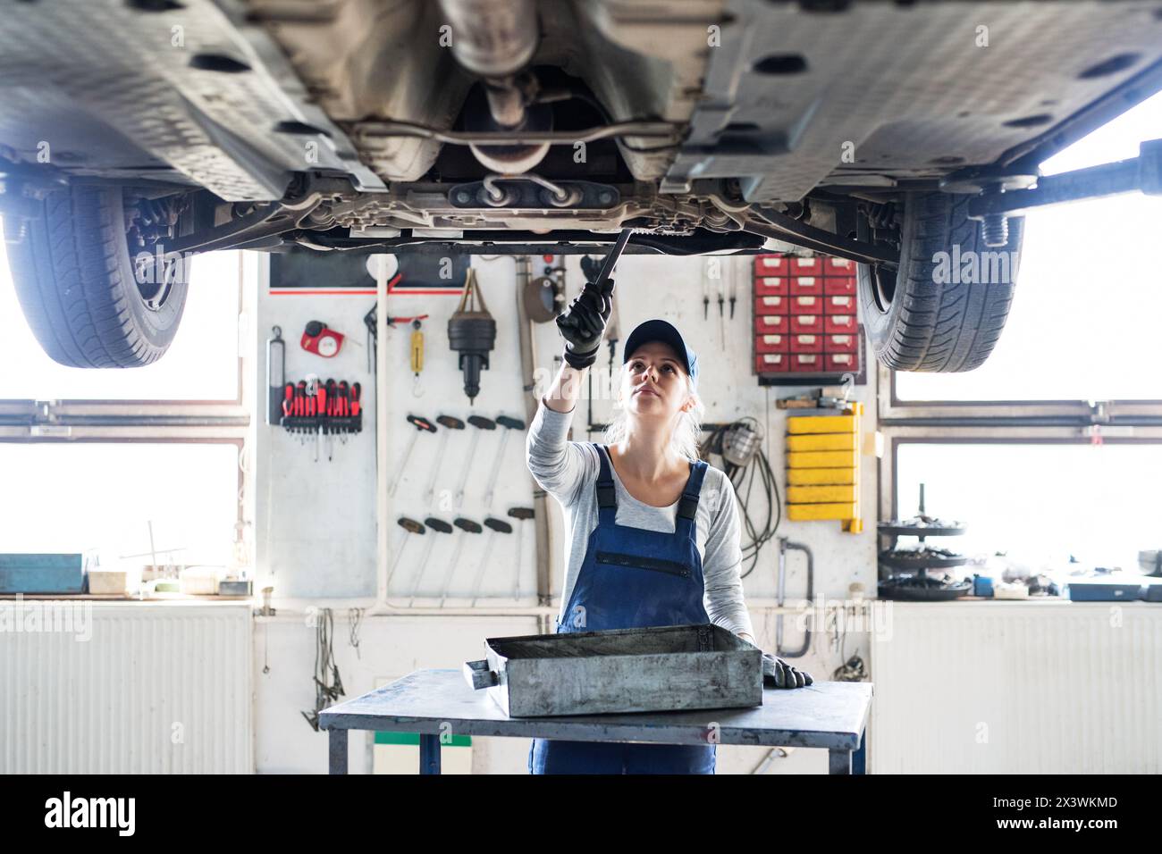 Female auto mechanic elevating car on car lift, changing oil. Beautiful ...