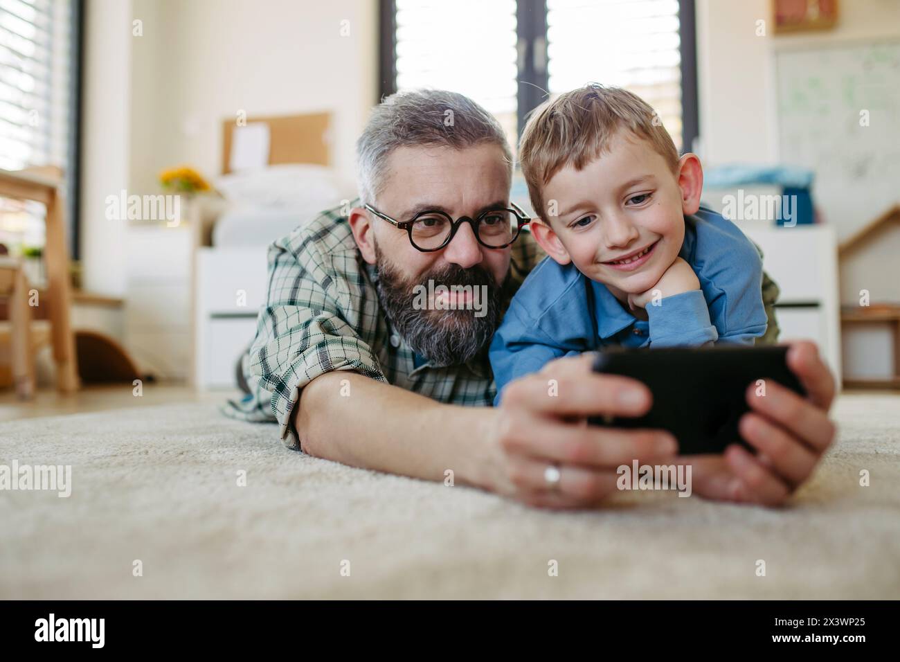 Little boy making selfie on smartphone with father, lying on floor in ...
