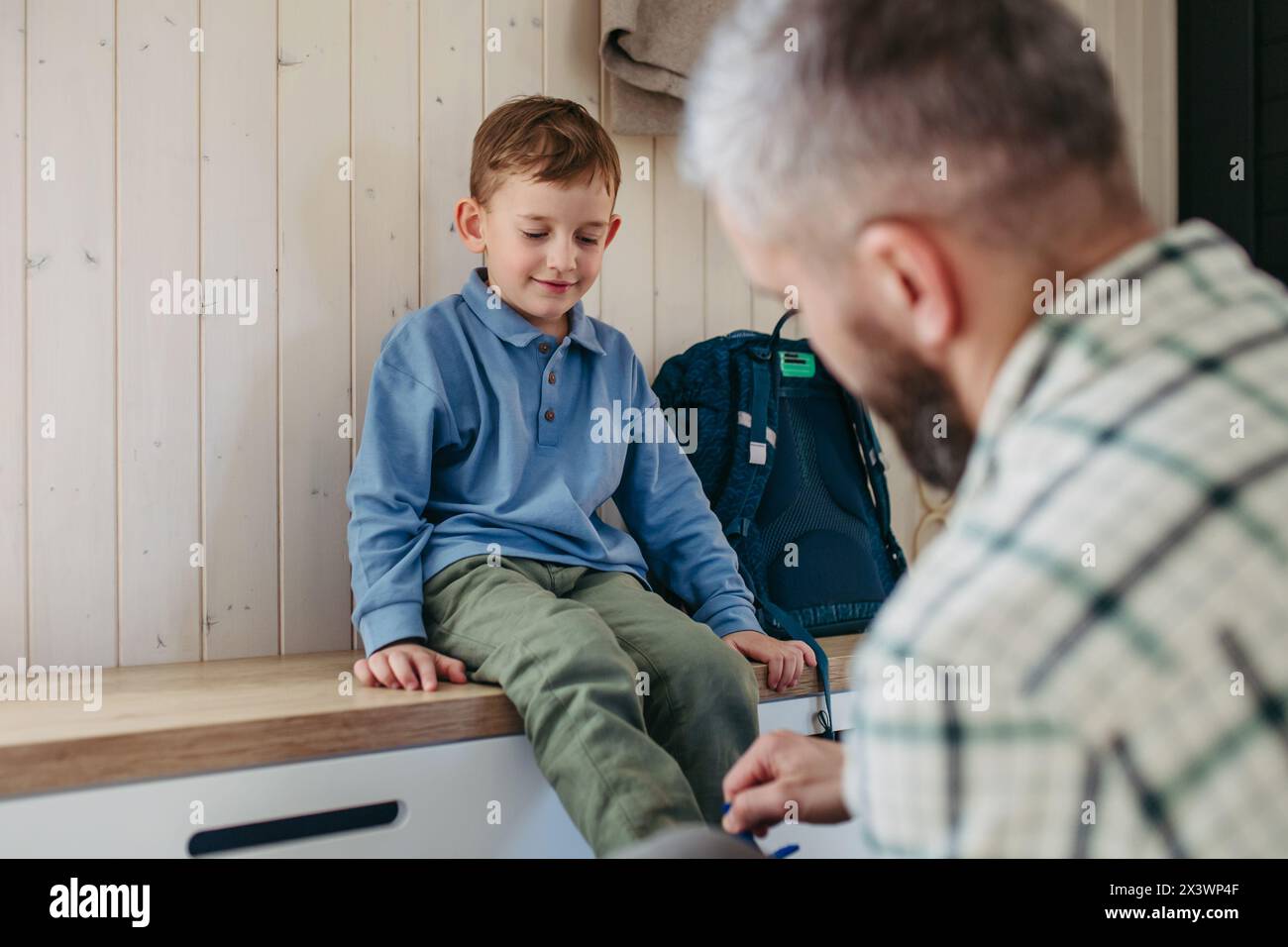 Father helping son get ready for kindergarten, preschool. Putting coat, shoes on, handing ...