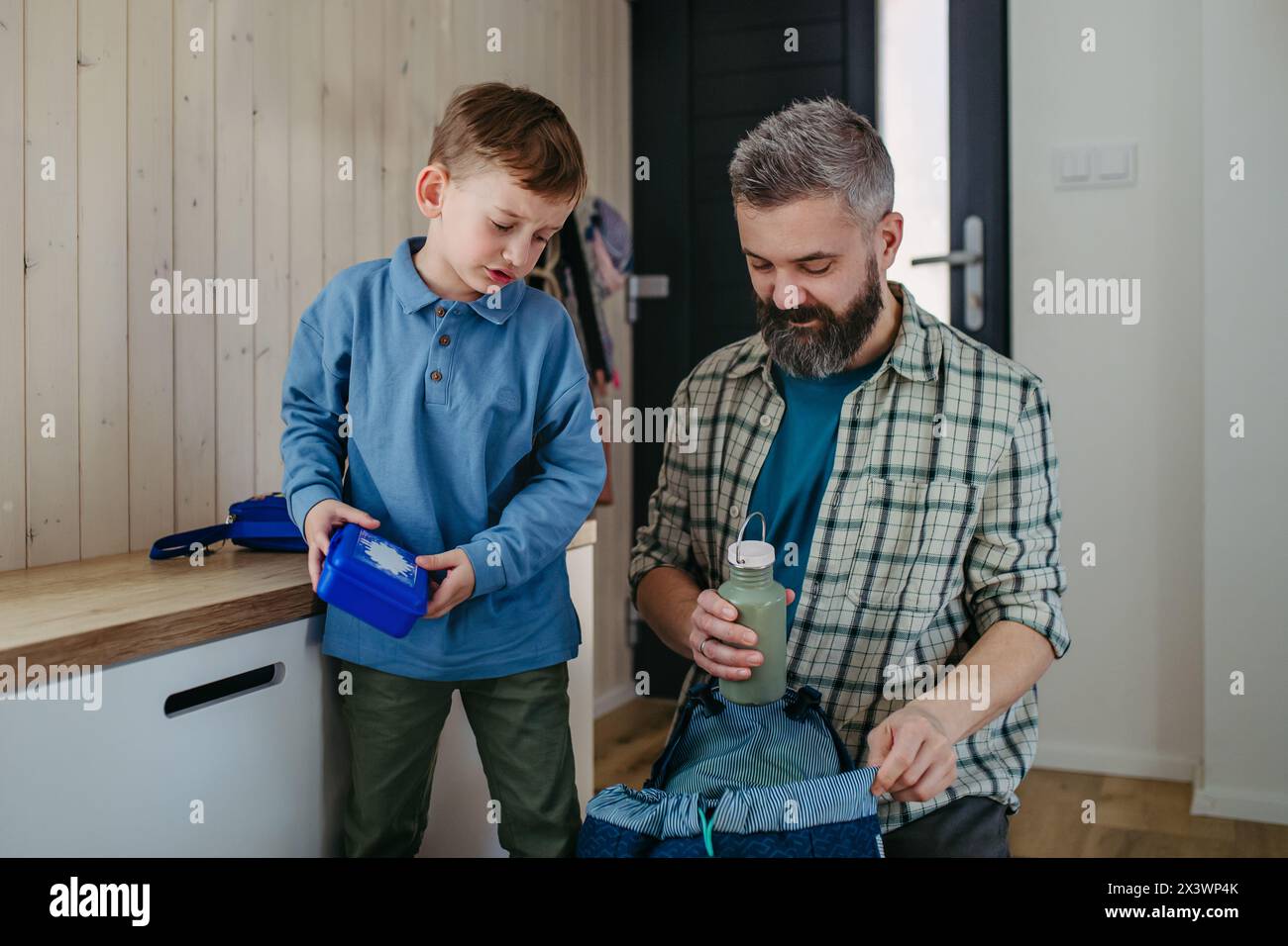 Father helping son get ready for kindergarten, preschool. Putting ...