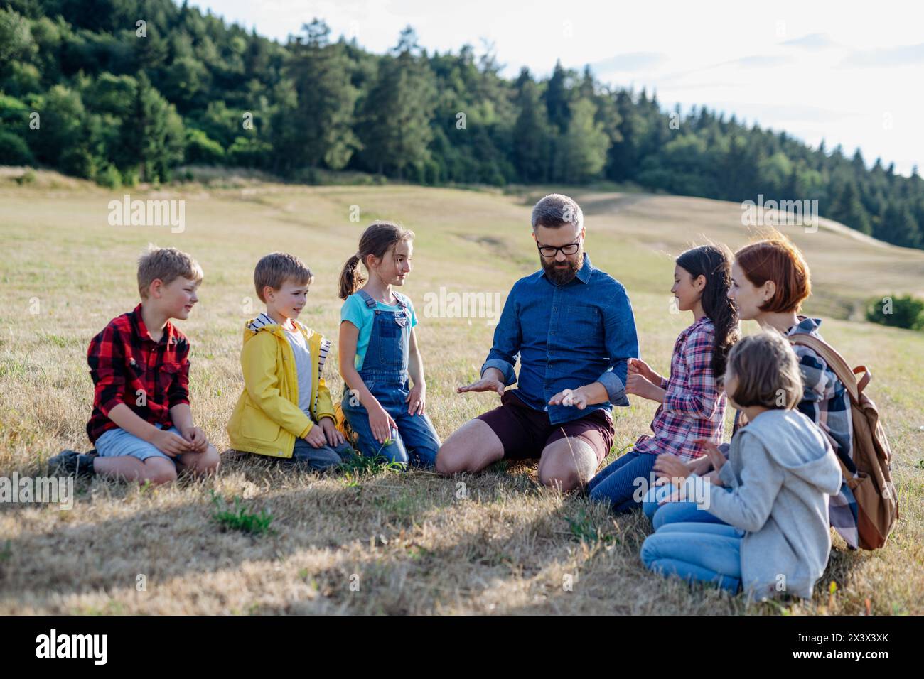 Children and teachers sitting on grass on meadow playing clapping game ...