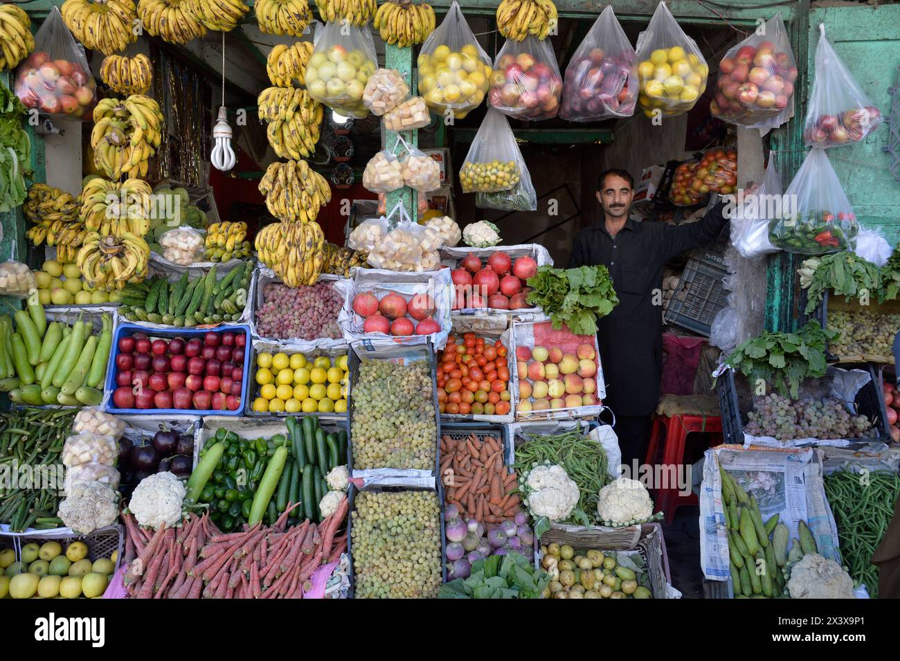 Pakistan, Gilgit, a man is posing in his vegetable and fruit colorful ...