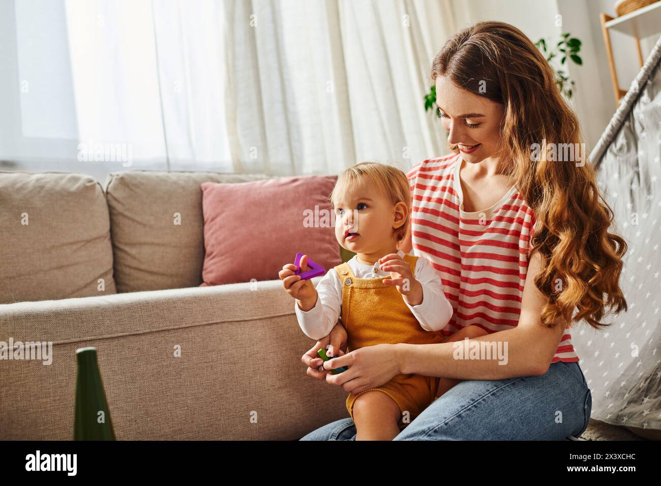A young mother sitting on a couch, cradling her toddler daughter in her ...