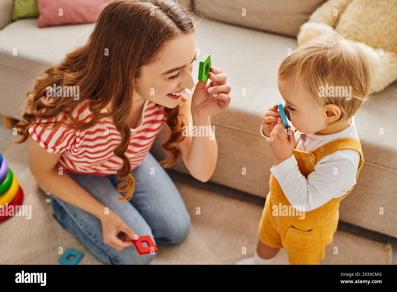 A young mother happily engages with her toddler daughter on the floor ...