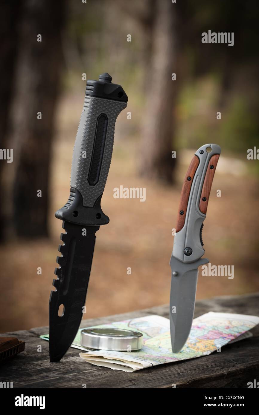 Two hunting knives are stuck in lid wooden table against background ...