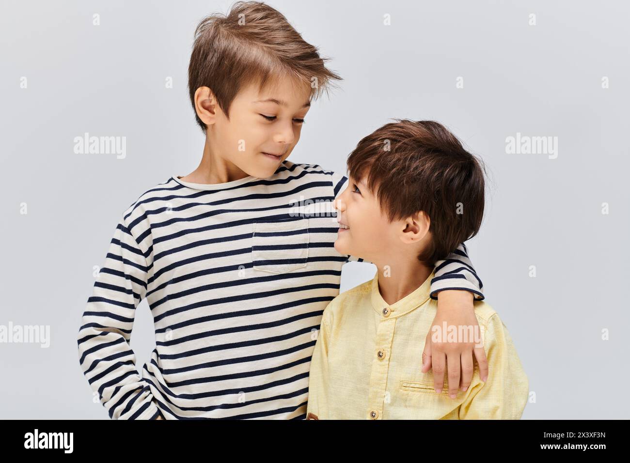 Two young Asian boys stand side by side in a studio setting on a grey ...