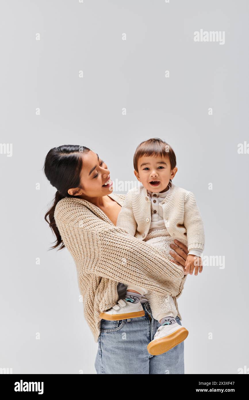 A young Asian mother cradling her baby in her arms in a studio against ...