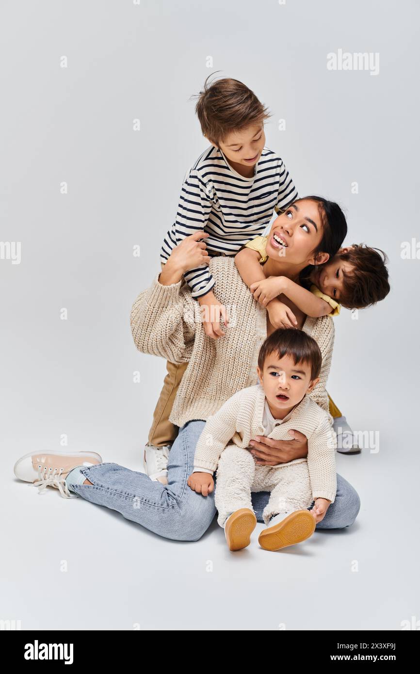 A young Asian mother and her children sit atop each other, creating a ...