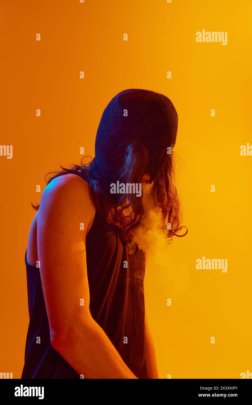 Punk rock. Young man with long hair, wearing black balaclava, smoking ...