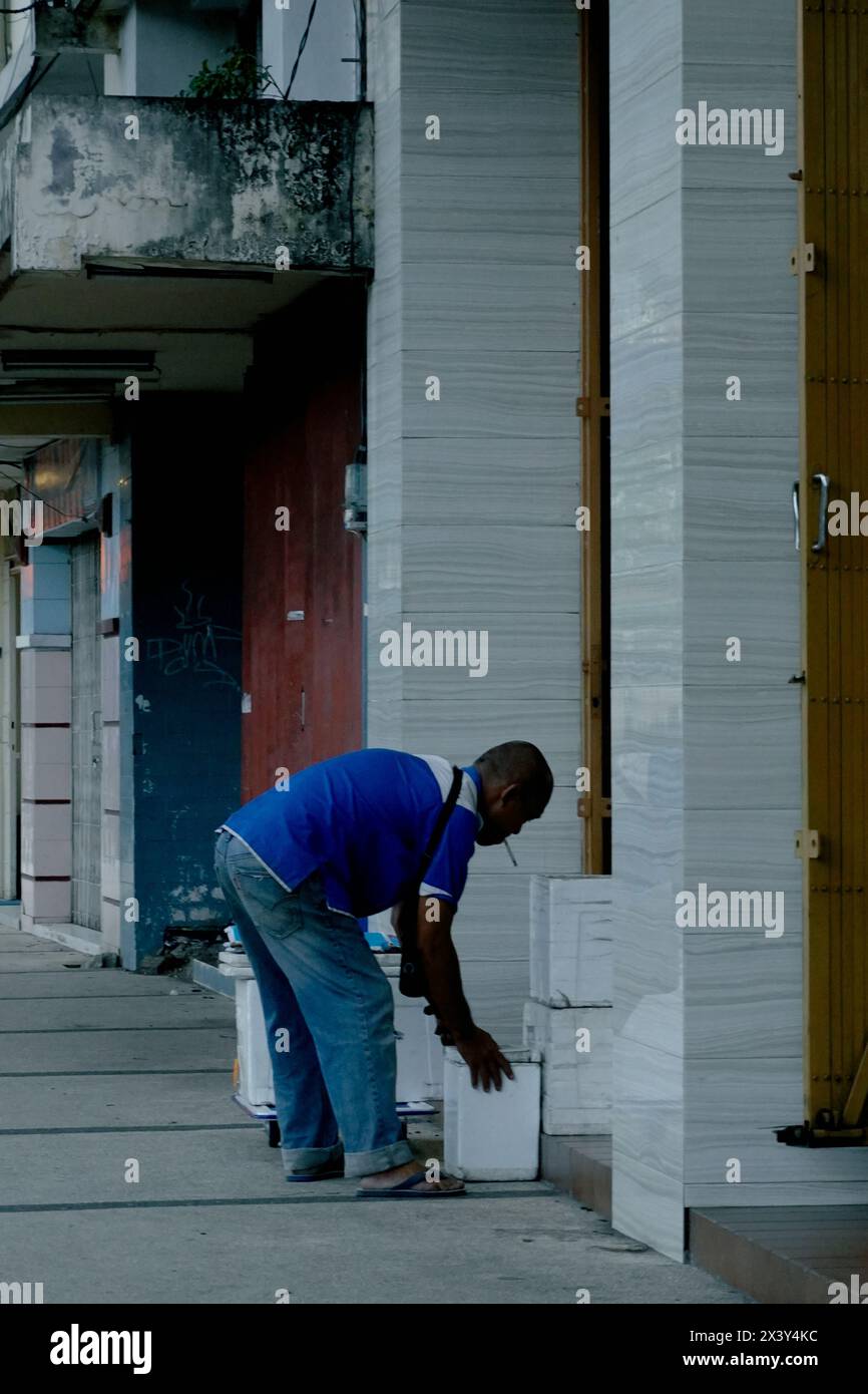 An old man was bending down to put things on the sidewalk near a ...