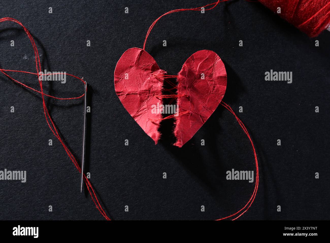 Halves of torn paper heart connected by thread on black background ...