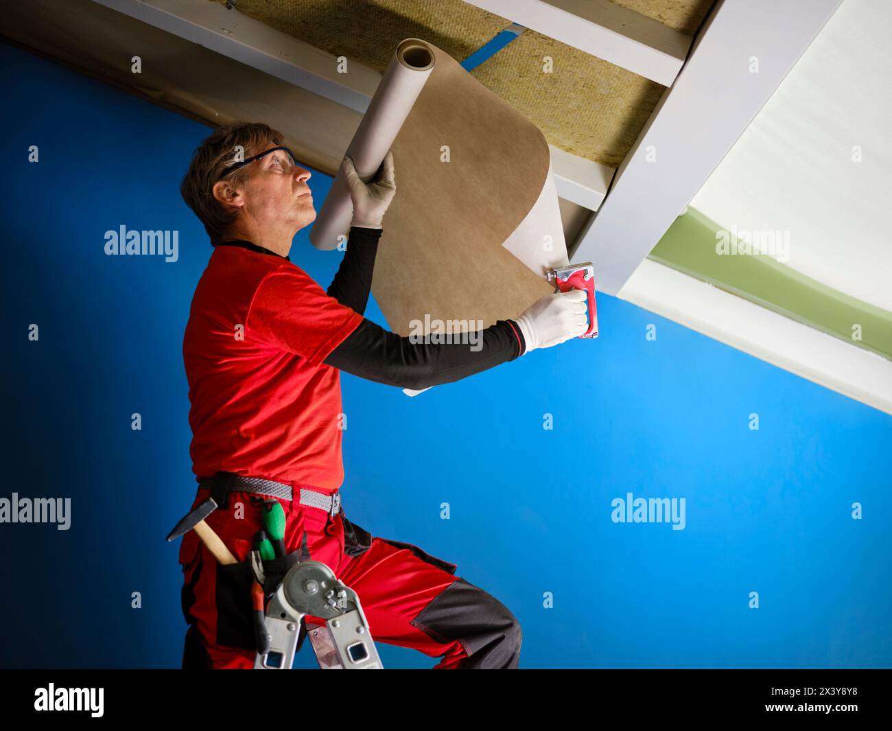 Craftsman in work clothes on a ladder, applies the anti-vapor sheet ...