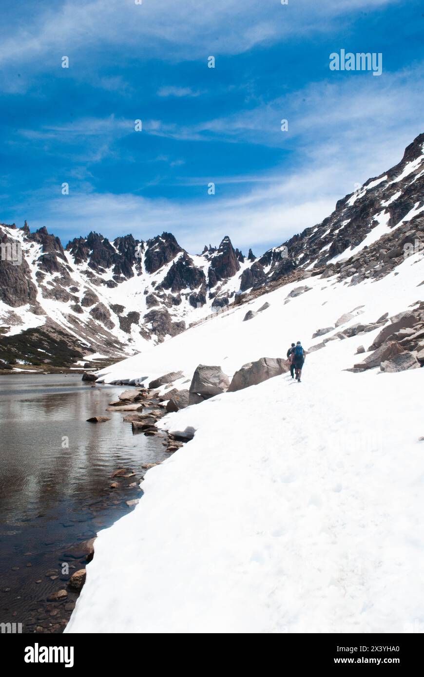 hikers trekking through snowy paths alongside a tranquil lake with ...