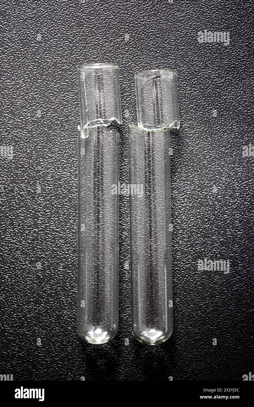 Close up of a pair of broken glass test tubes on a plastic black ...