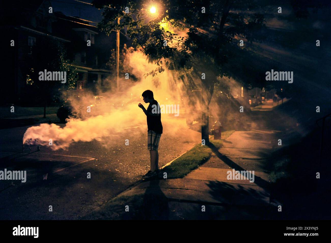 A young boy playing with fireworks in the middle of a neighborhood ...