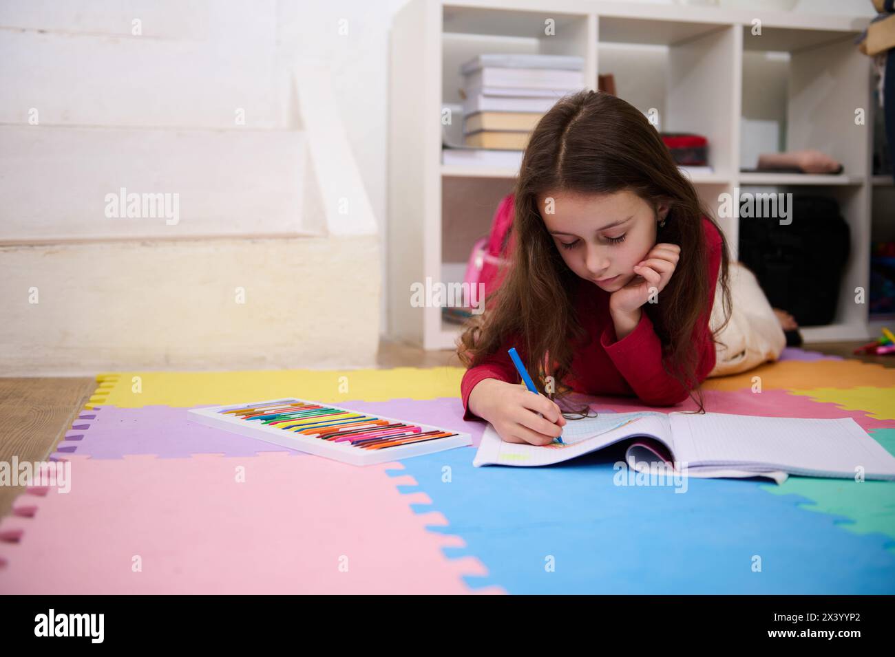 Smart small school girl studying at home, handwriting in notebook ...