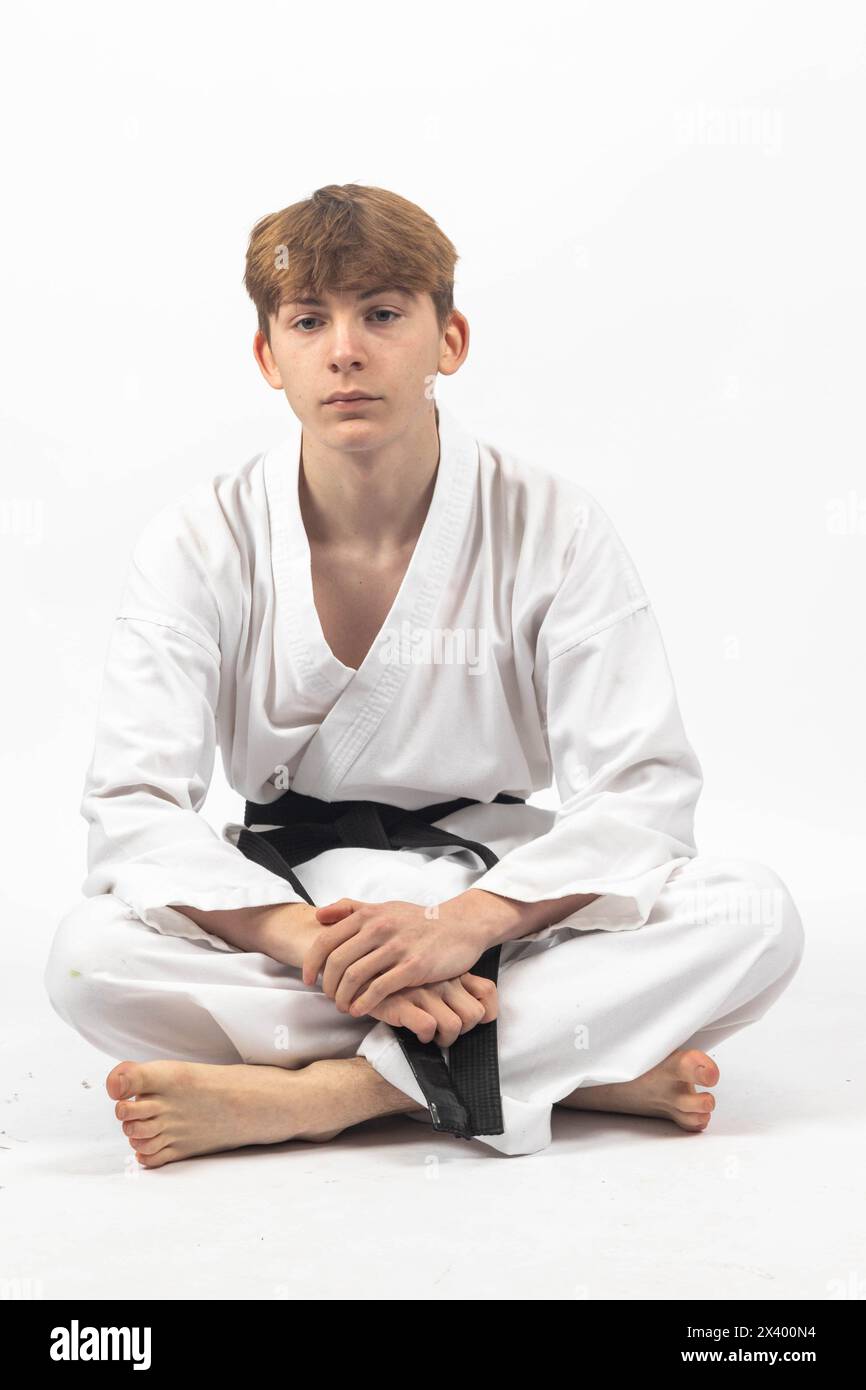 A 15 year old Karate Blackbelt boy, wearing A Gi sitting cross legged ...