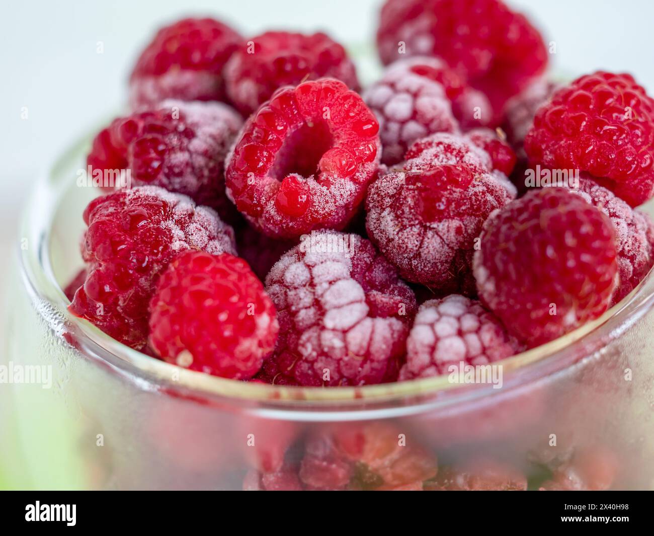 raspberries frozen in a glass dish, side view, visible frost on red ...