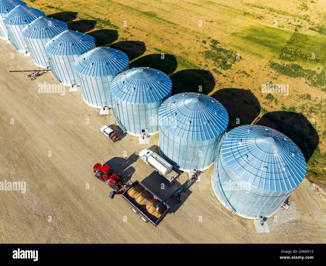 Aerial view of a row of large metal grain bins with tractor and grain ...