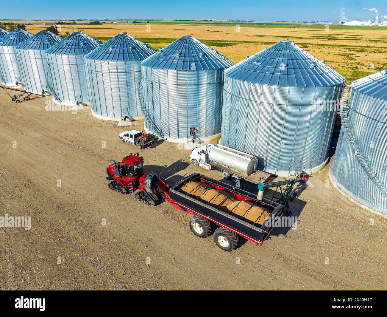 Aerial view of a row of large metal grain bins with tractor and grain ...