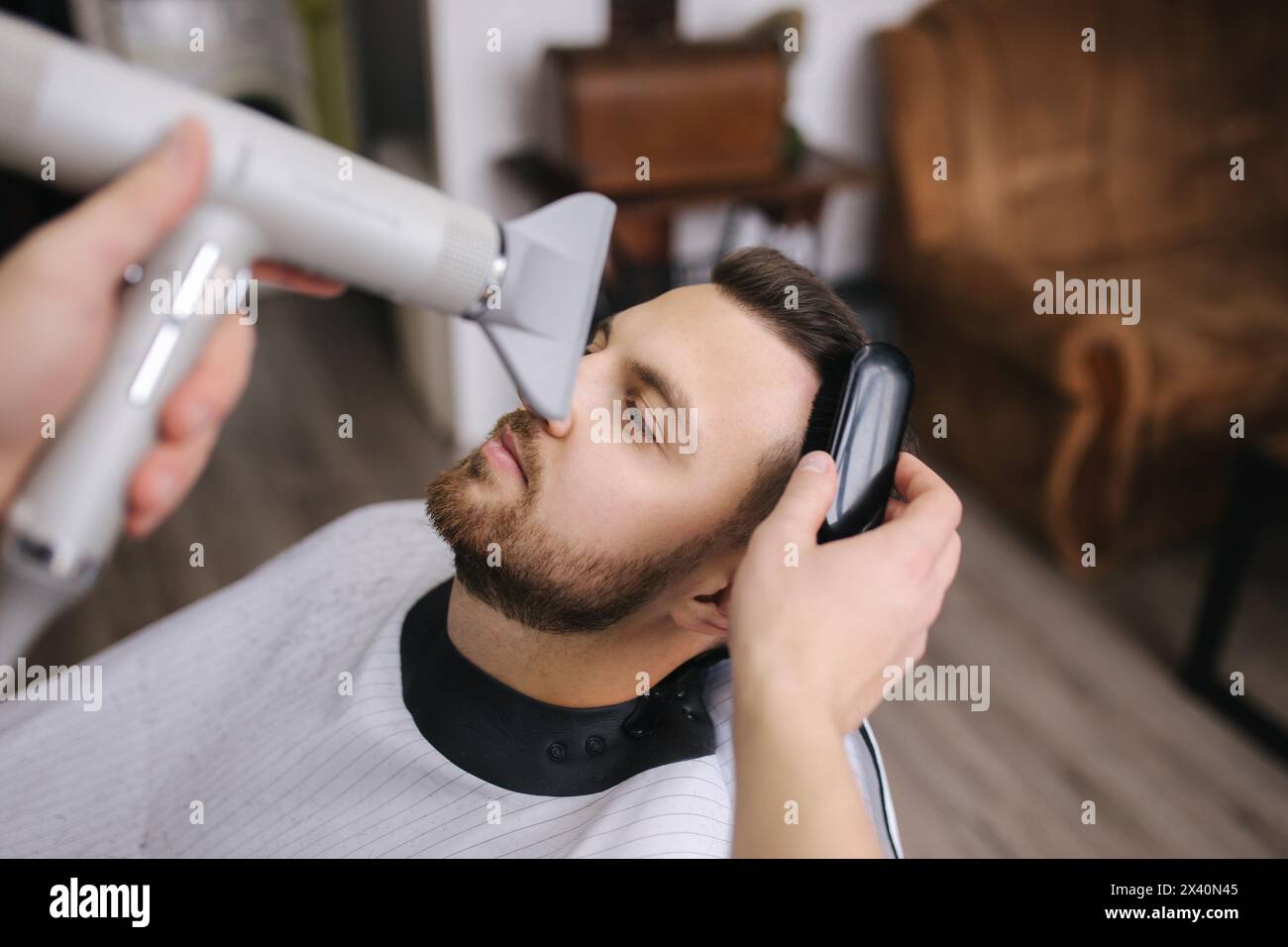 Hairdresser uses a hair dryer and comb to style the hair. Client in ...
