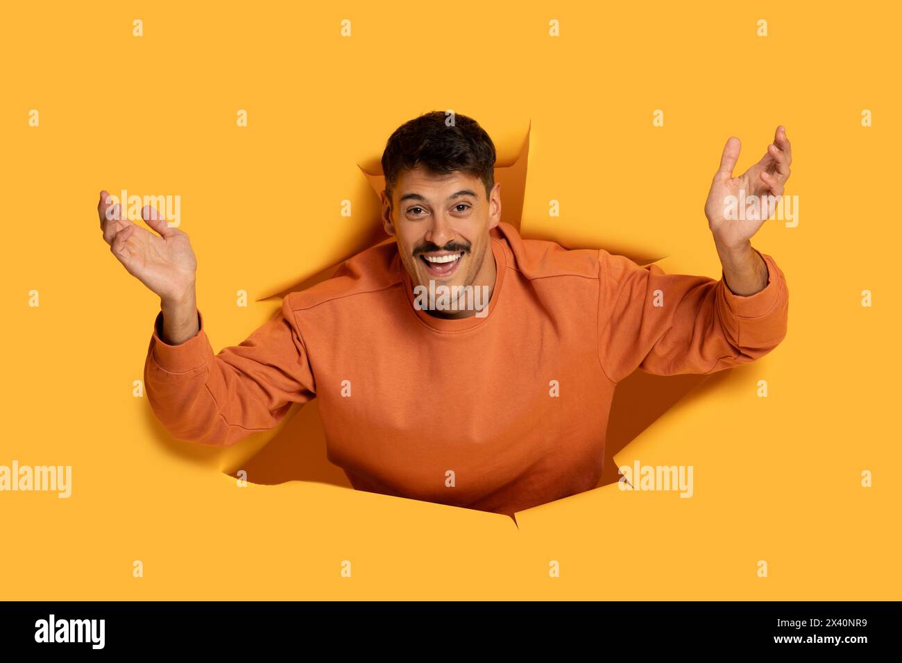 Joyful Man Popping Through Orange Paper Background With Hands Raised ...