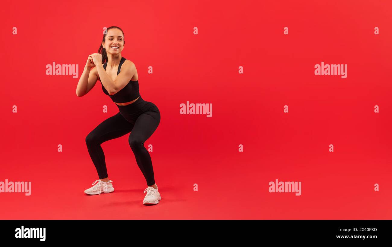 Smiling Woman Engages in a Squat Exercise Against Red Stock Photo - Alamy