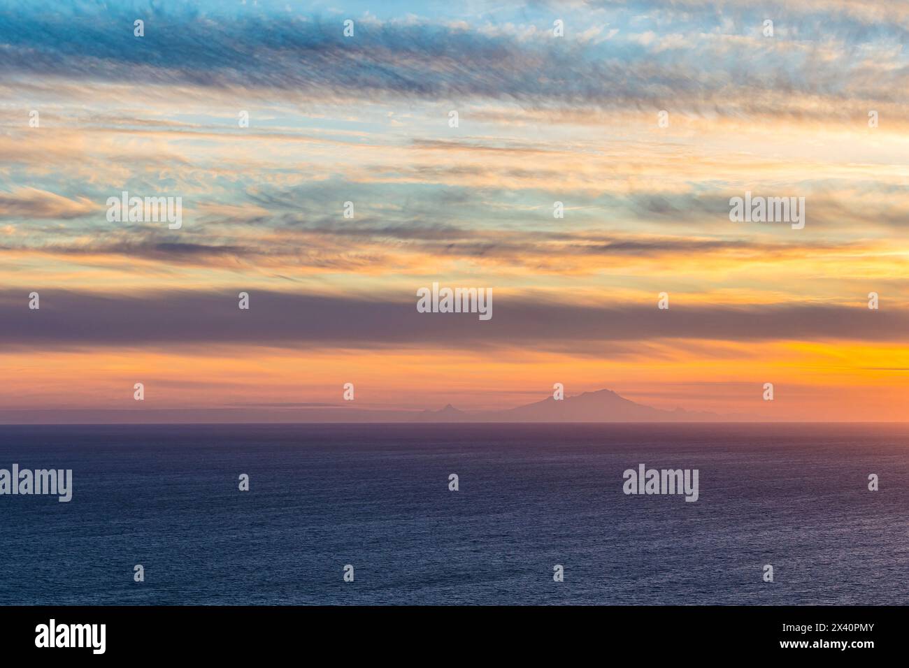 Beautiful sunset over ocean with silhouetted mountains in the distance ...